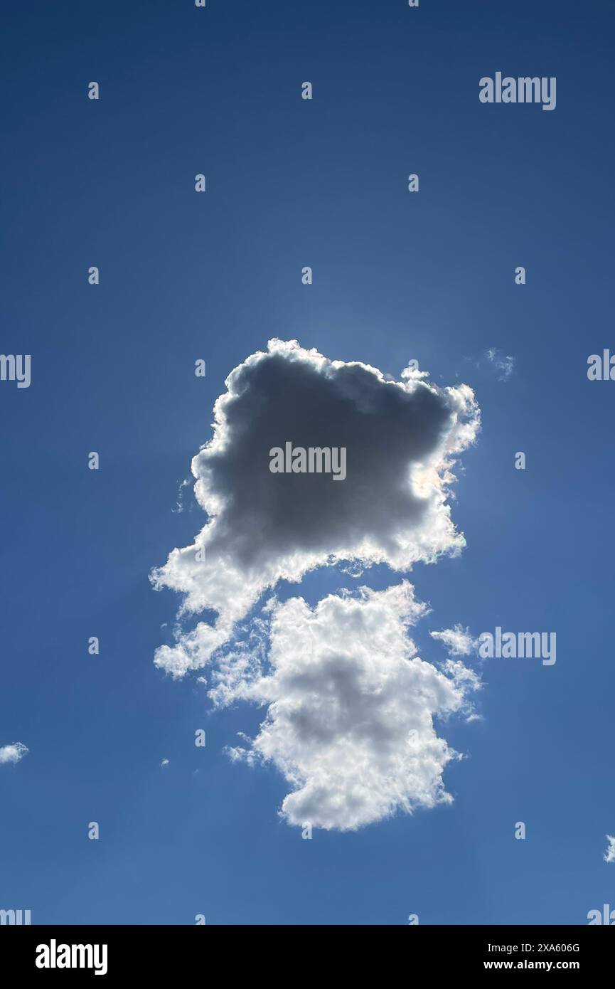 The sun behind a cloud against a clear blue sky casting out light from ...