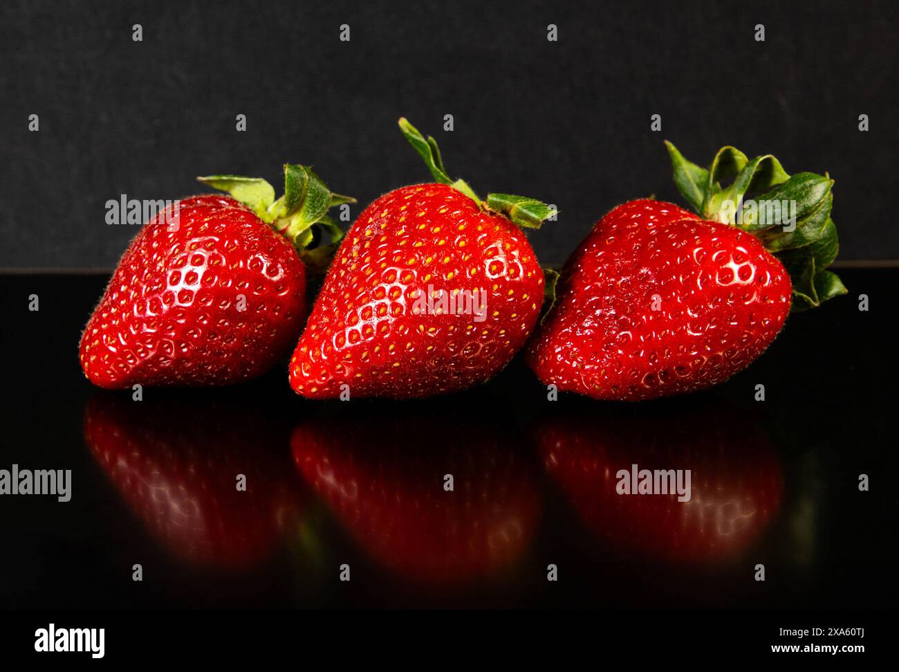 Three ripe strawberries arranged in a line on a tabletop Stock Photo ...