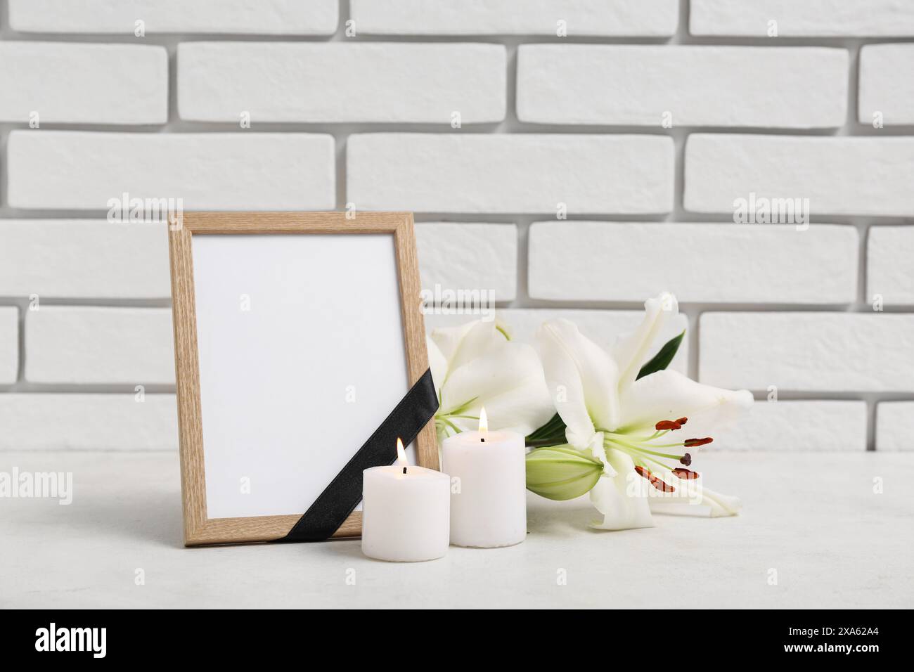 Blank funeral photo frame, candles and flowers on white brick ...