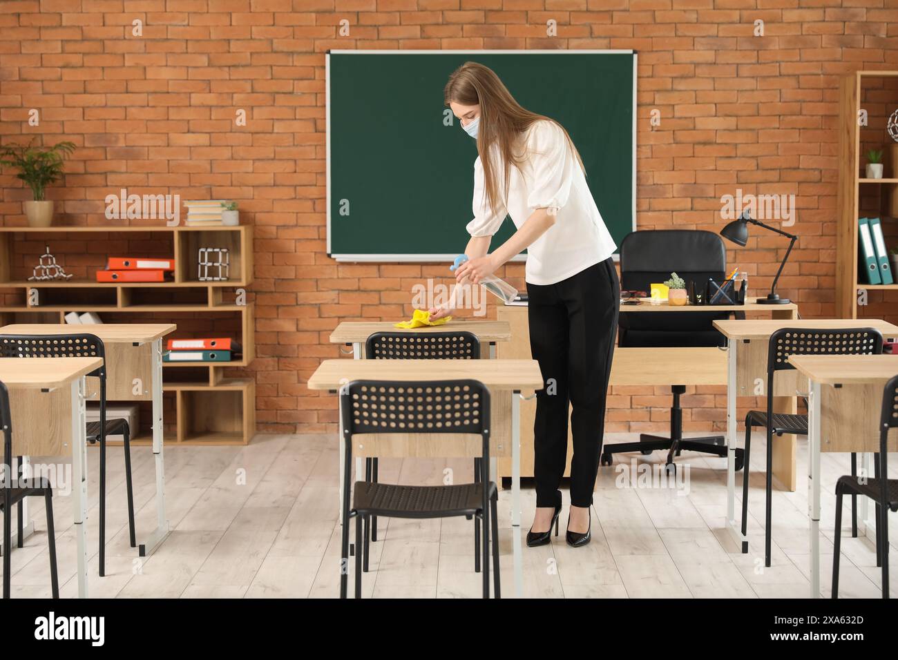 Female teacher with medical mask cleaning table in classroom Stock ...