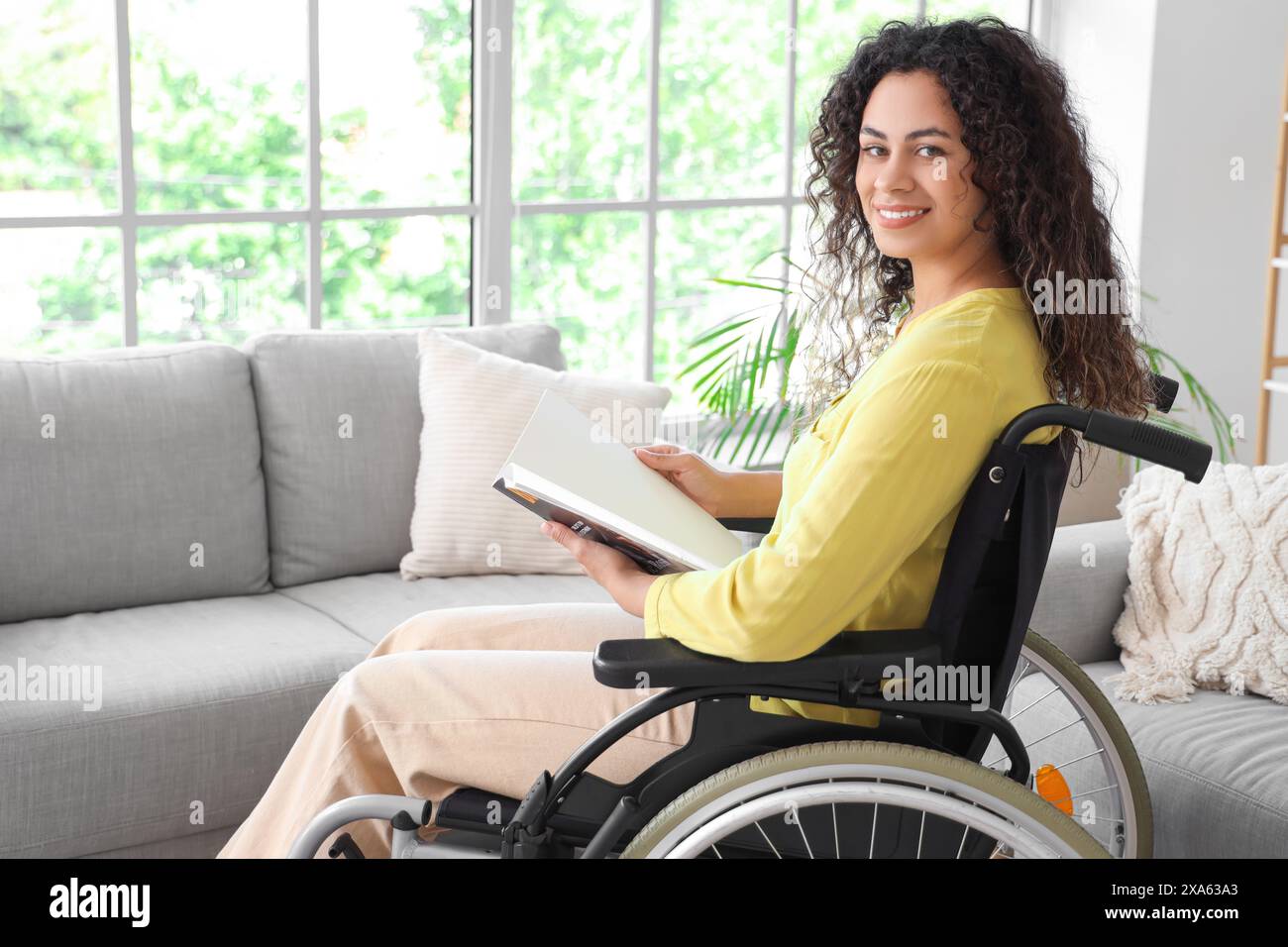 Young African-American woman in wheelchair reading magazine at home ...