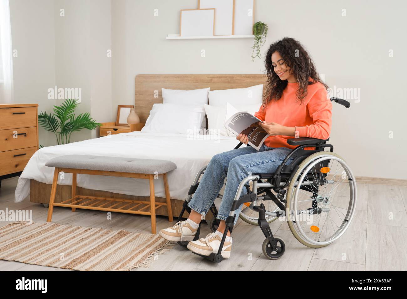 Young African-American woman in wheelchair reading magazine at home ...
