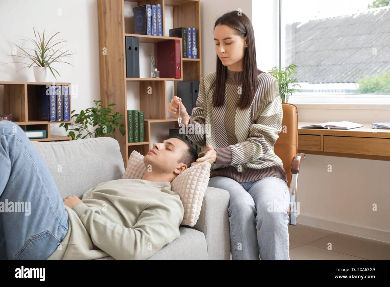 Female psychologist with pendulum hypnotizing man in office Stock Photo ...