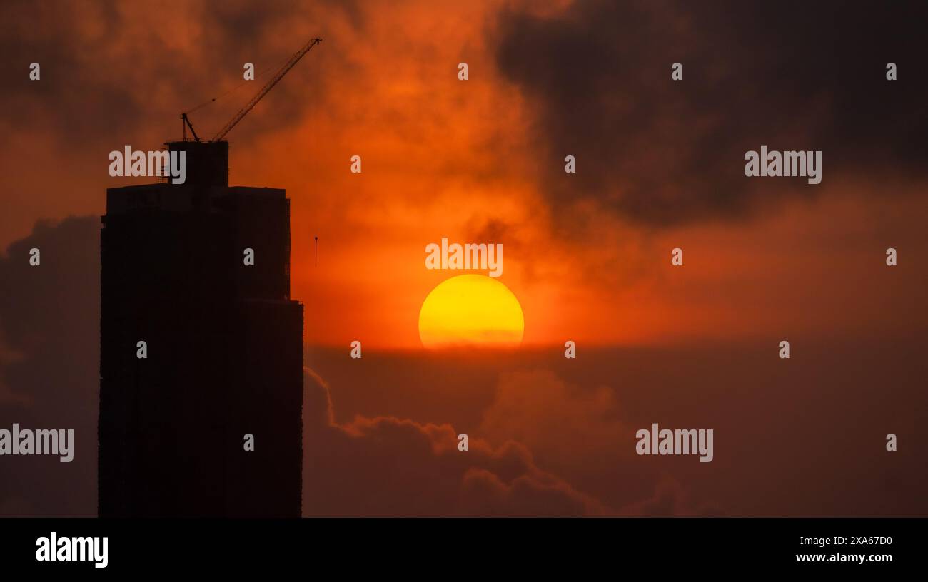 The sun sets behind skyscraper with crane in foreground Stock Photo - Alamy