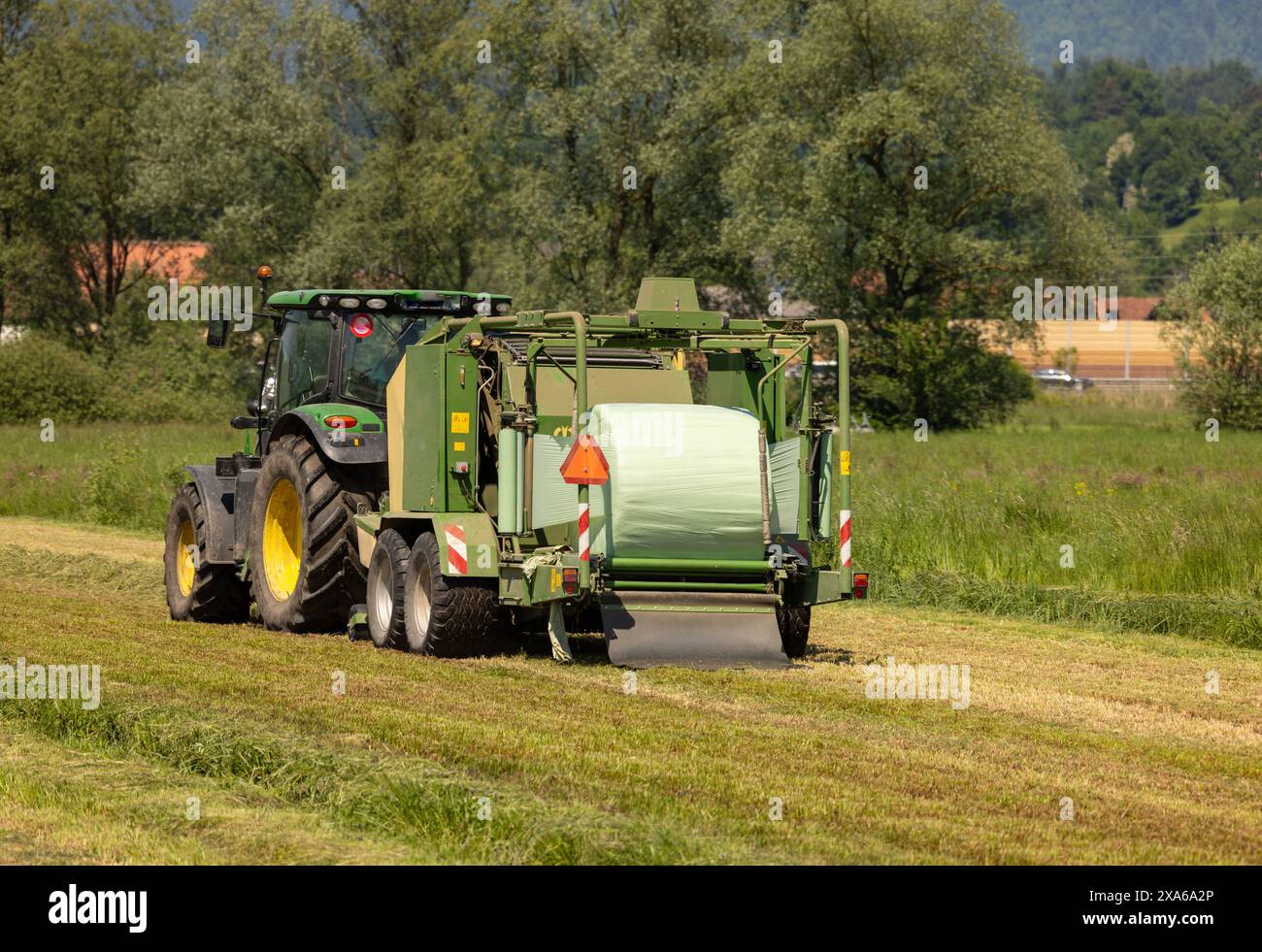 A tractor cultivating a field surrounded by green grass Stock Photo - Alamy