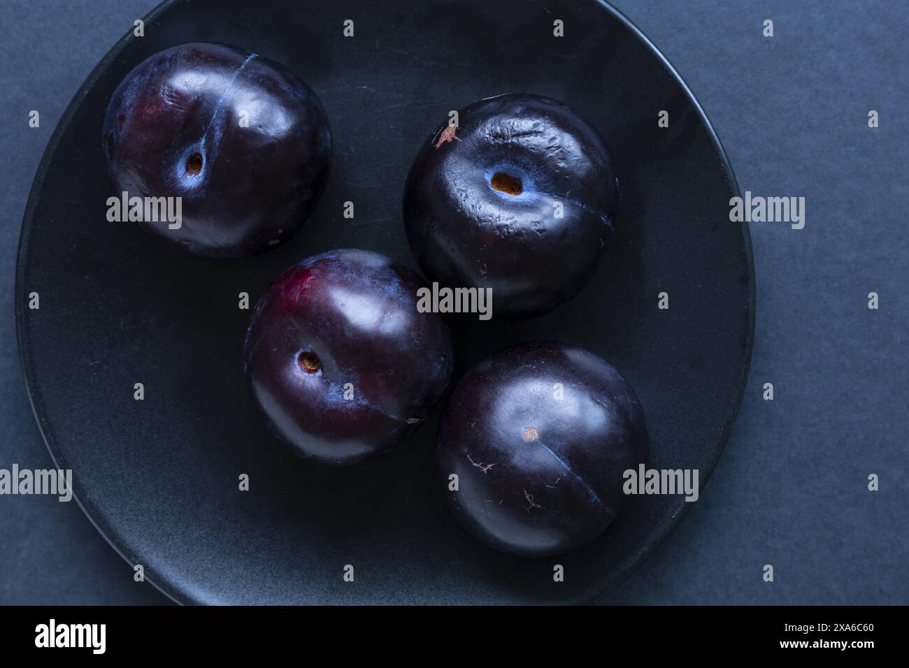 close-up tabletop photo of dark blue plum fruits in a black ceramic ...
