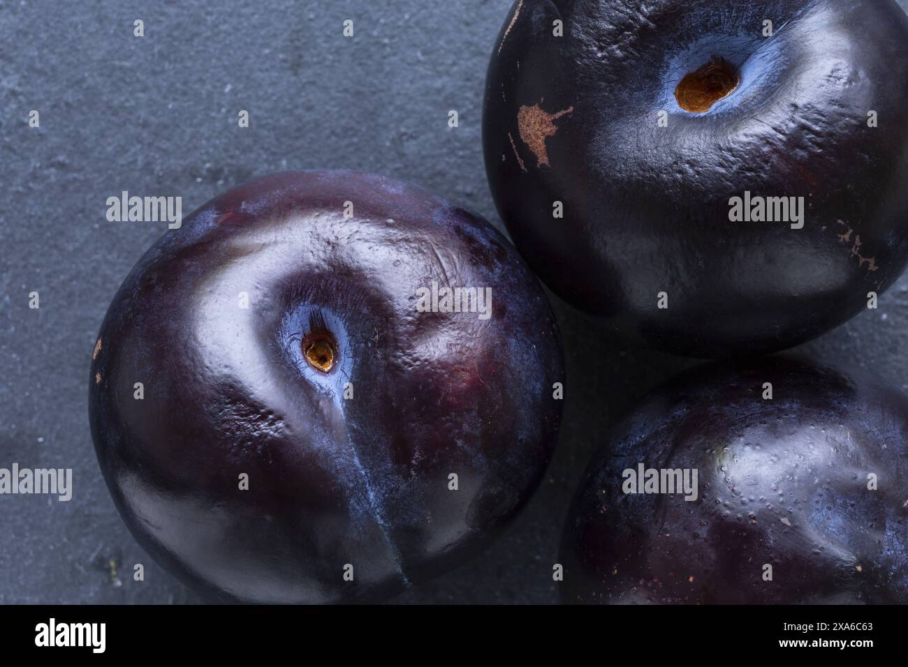 close-up tabletop macro photo of dark blue plum fruits on a dark ...