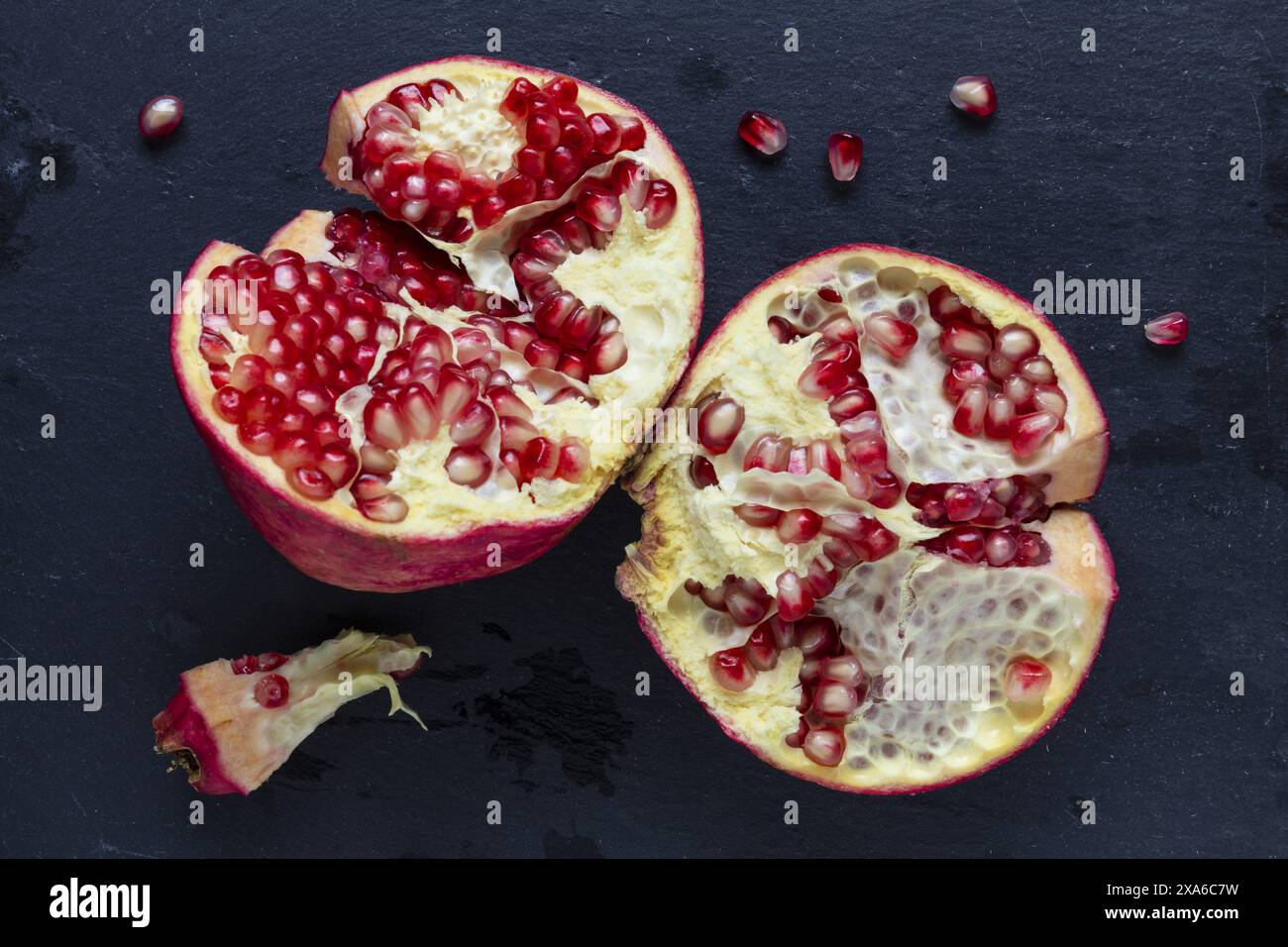 close-up tabletop photo of an open in half pomegranate on a dark black ...