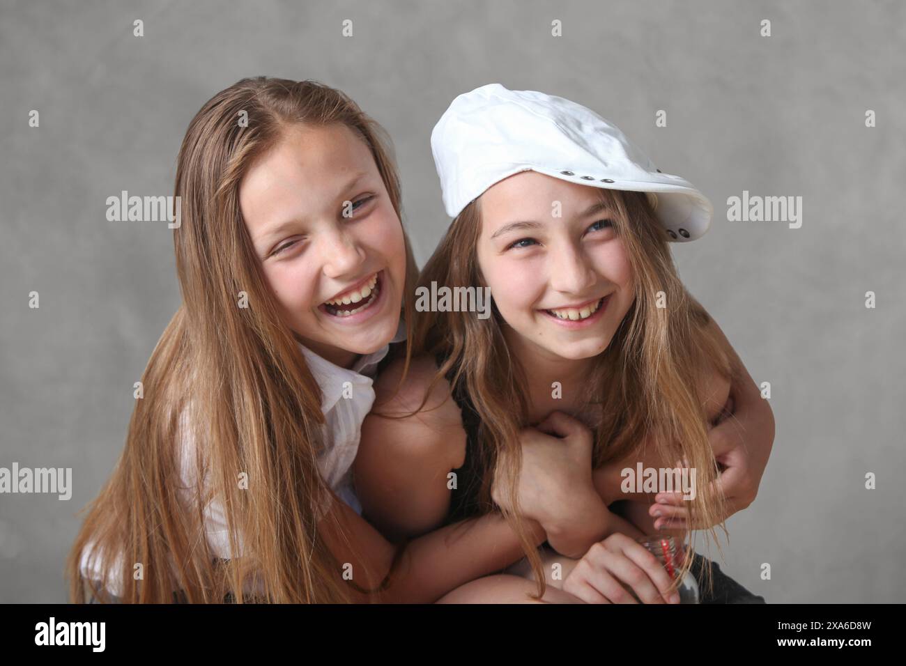 two cute cheerful preteen girls laughing and hugging on grey background ...