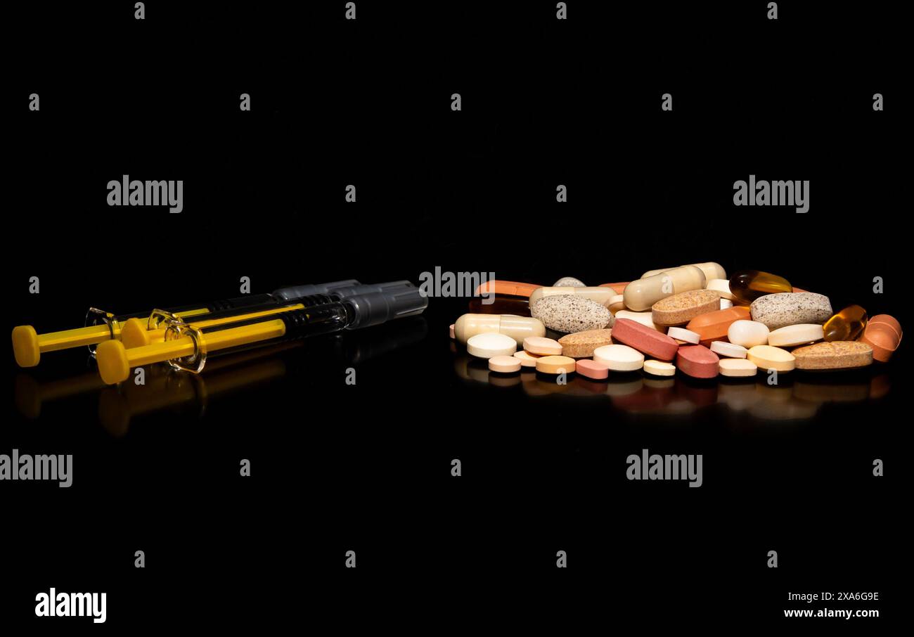 A close-up of some syringes and a pile of different medicine tablets on ...