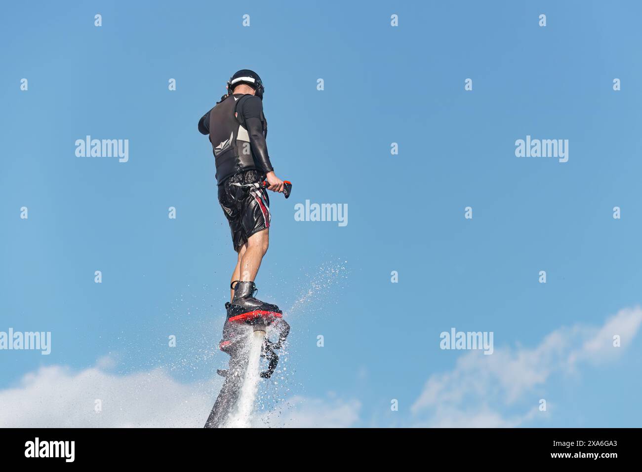 Daring individual soars above water on a jetpack, with a clear blue sky ...