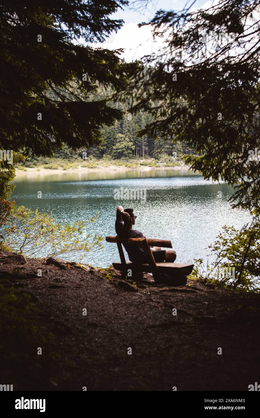 A person sitting on a bench gazing at water near a park bench Stock ...