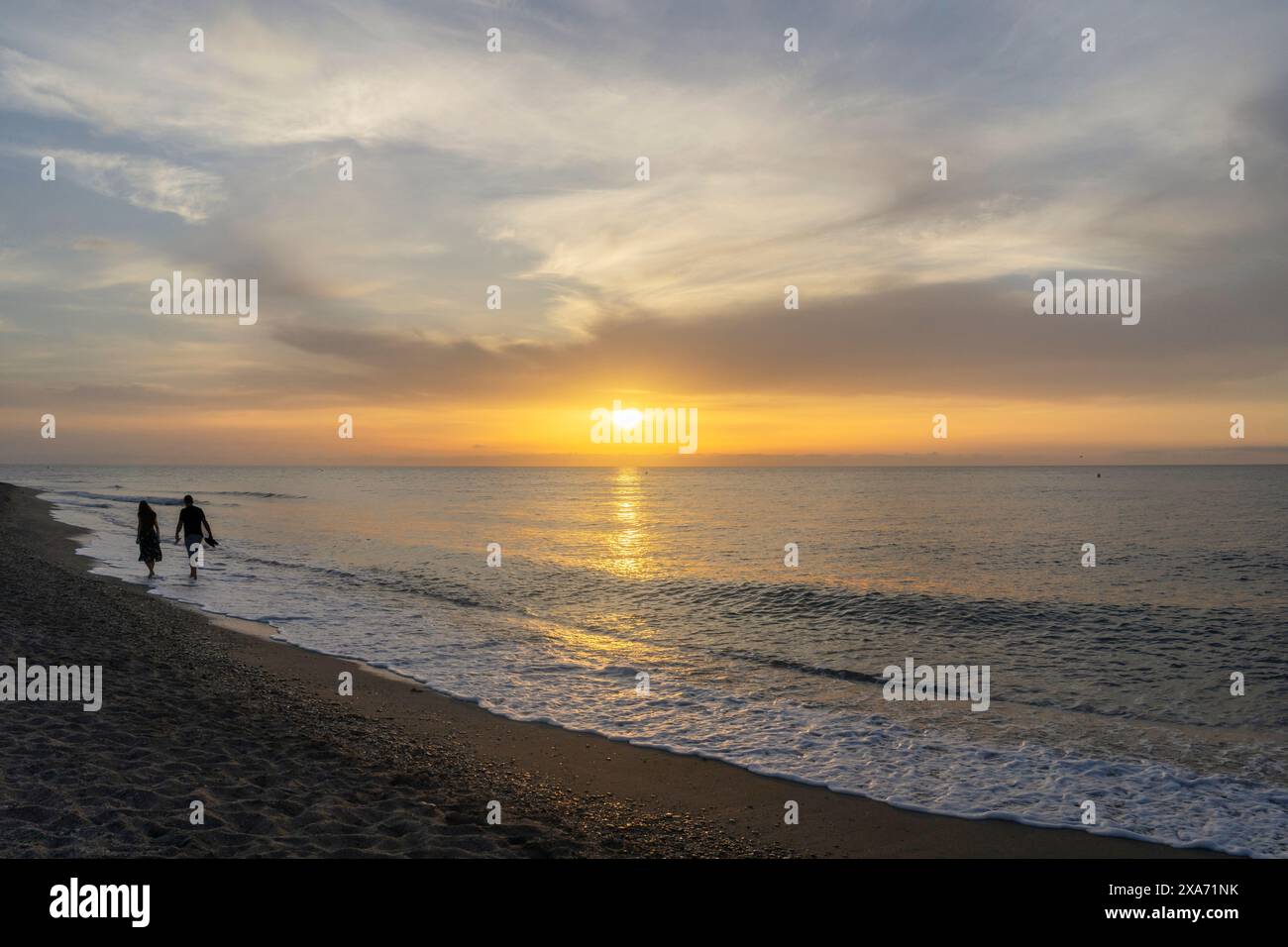 A couple in swimsuits, seen from behind, stroll along the shore of the beach, enjoying a ...