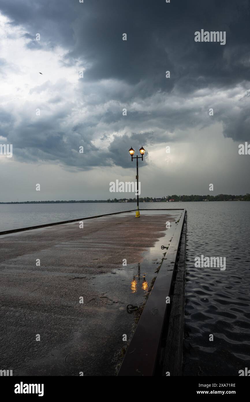 Storm clouds circle above a pier with a dark dramatic light post ...
