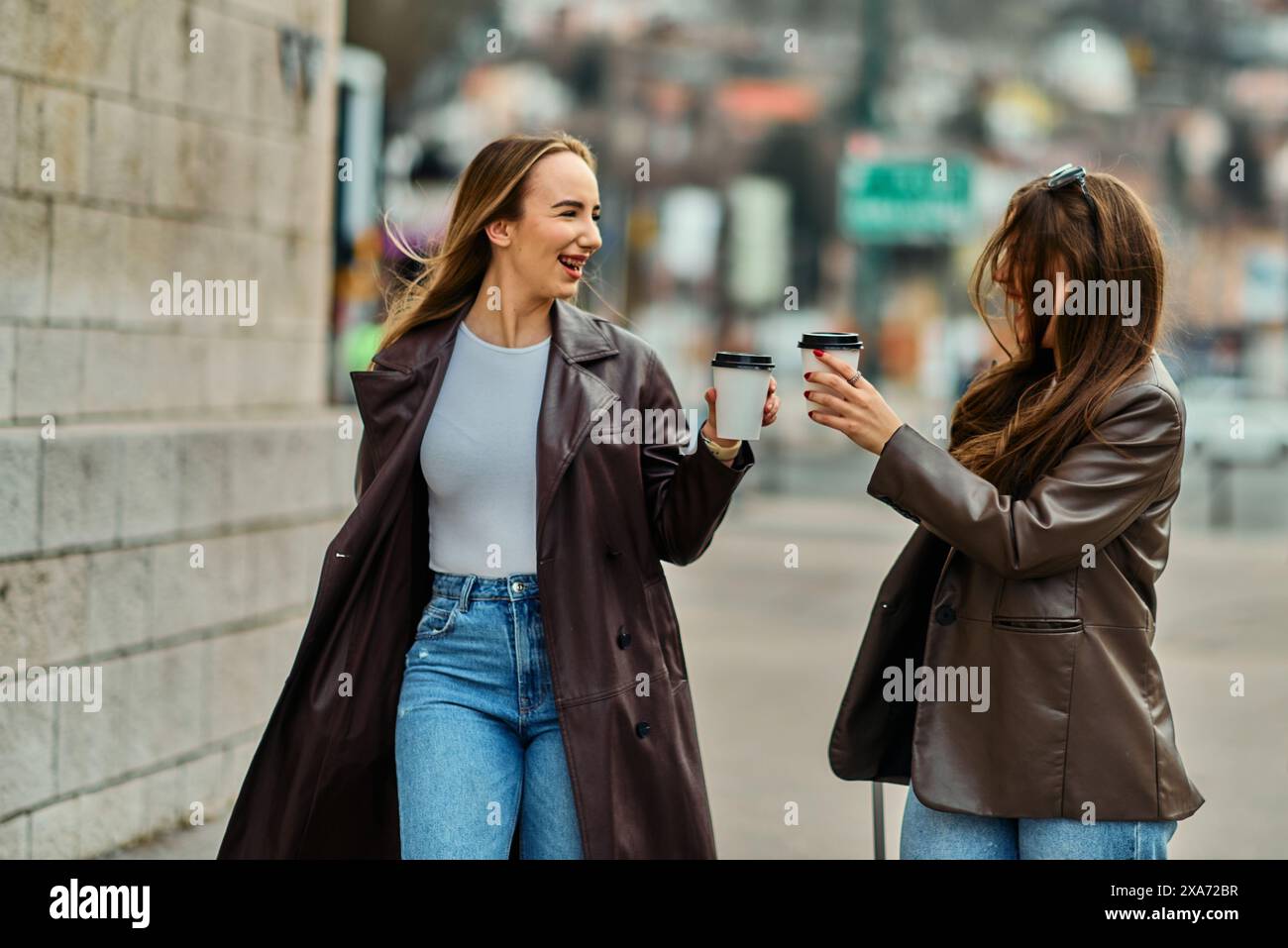 Two beautiful business women go to work while holding cups of coffee in ...