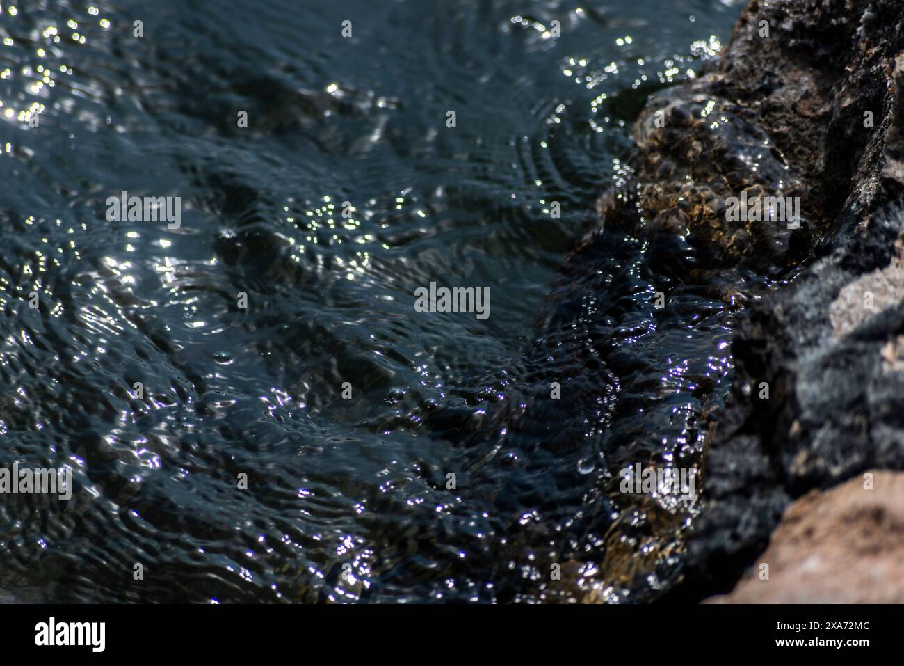 Sunlight glistens on water streaming through rocks Stock Photo - Alamy