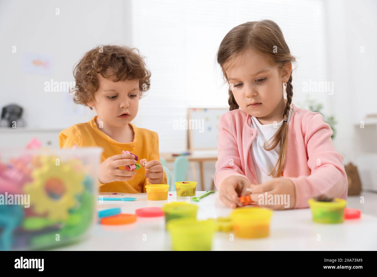 Cute little children modeling from plasticine at white table in ...
