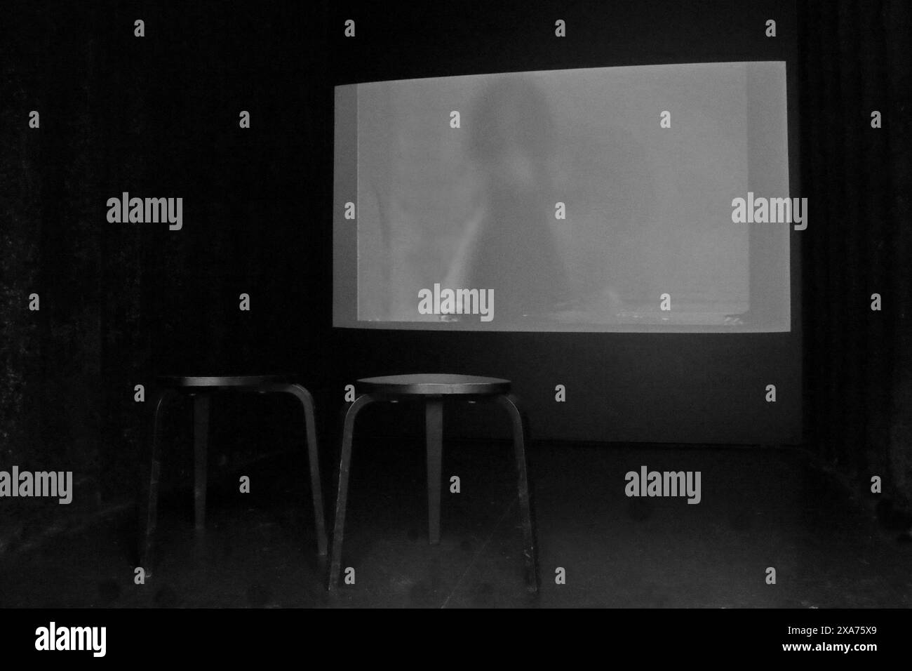 A black and white shot of an empty dark room with two benches in front ...