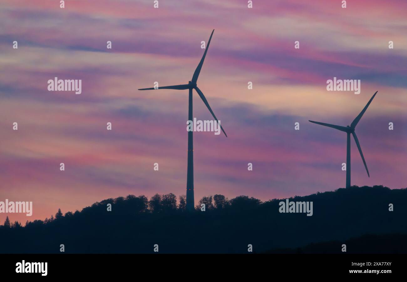 Two wind turbines silhouetted against a sunset sky with purple, pink ...