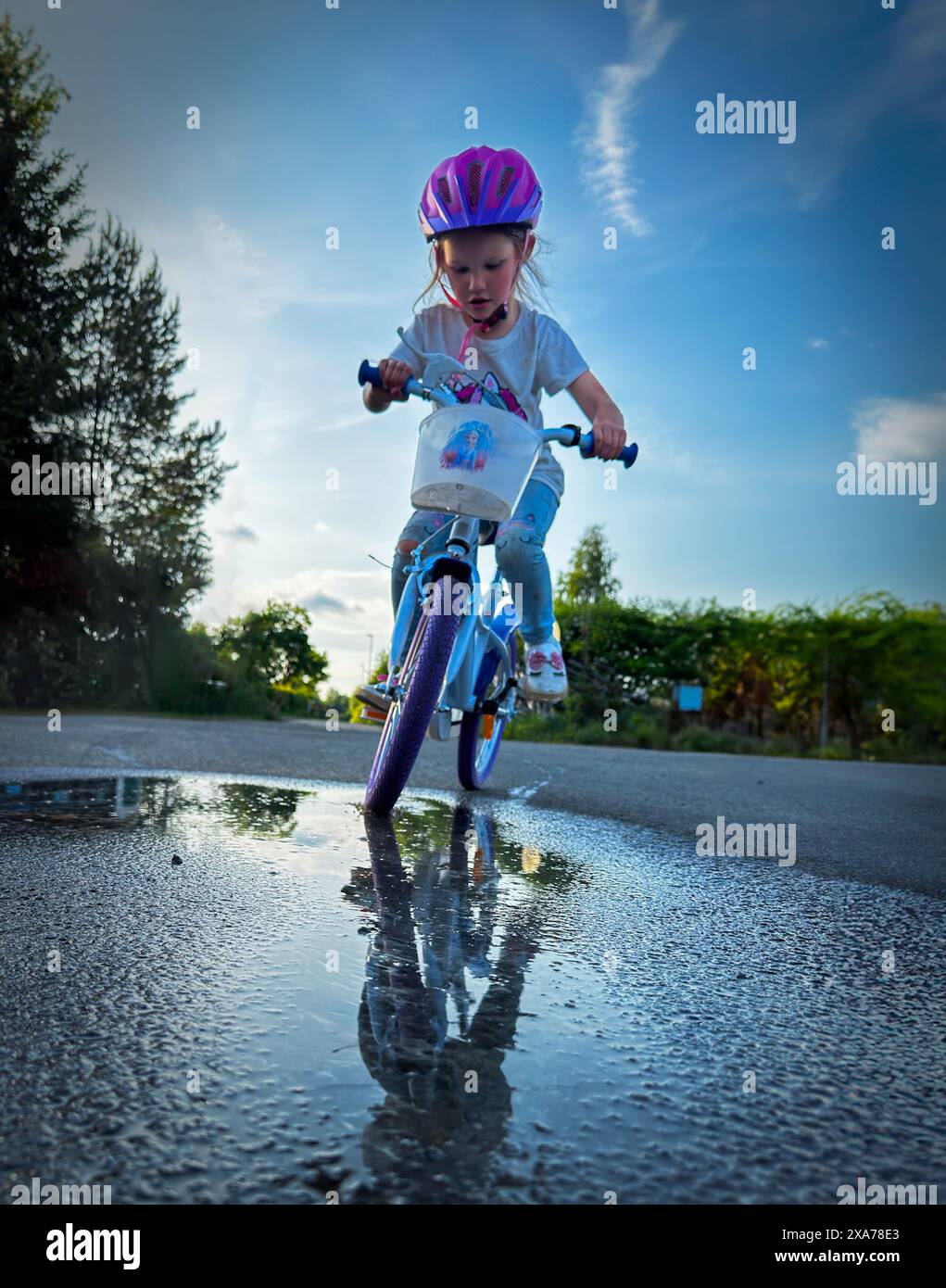 A young girl riding a small bicycle in a rain puddle on a road during ...