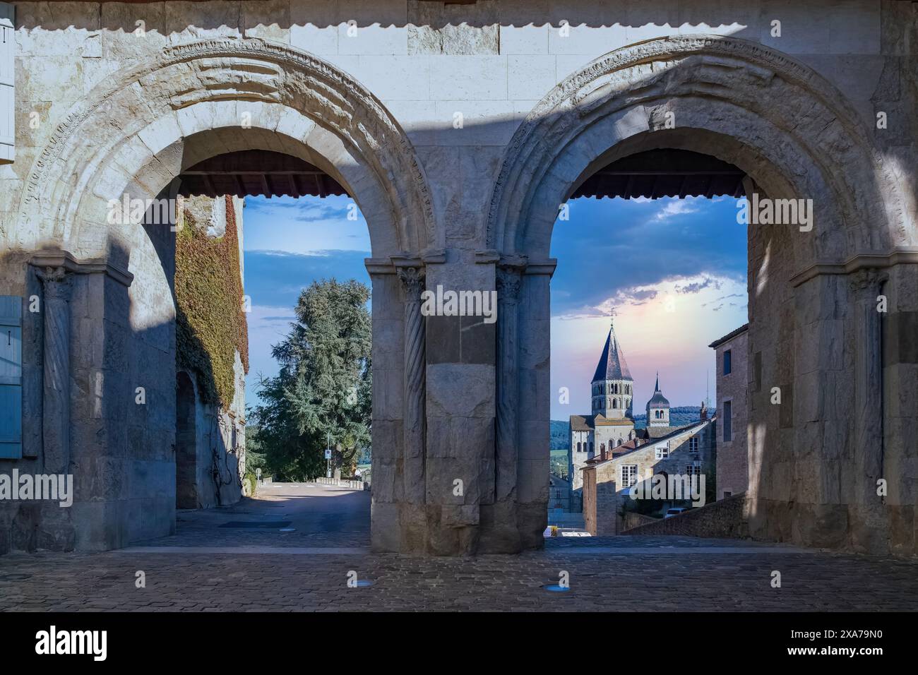 The historic Cluny Abbey monastery through a stone arch at sunset in ...