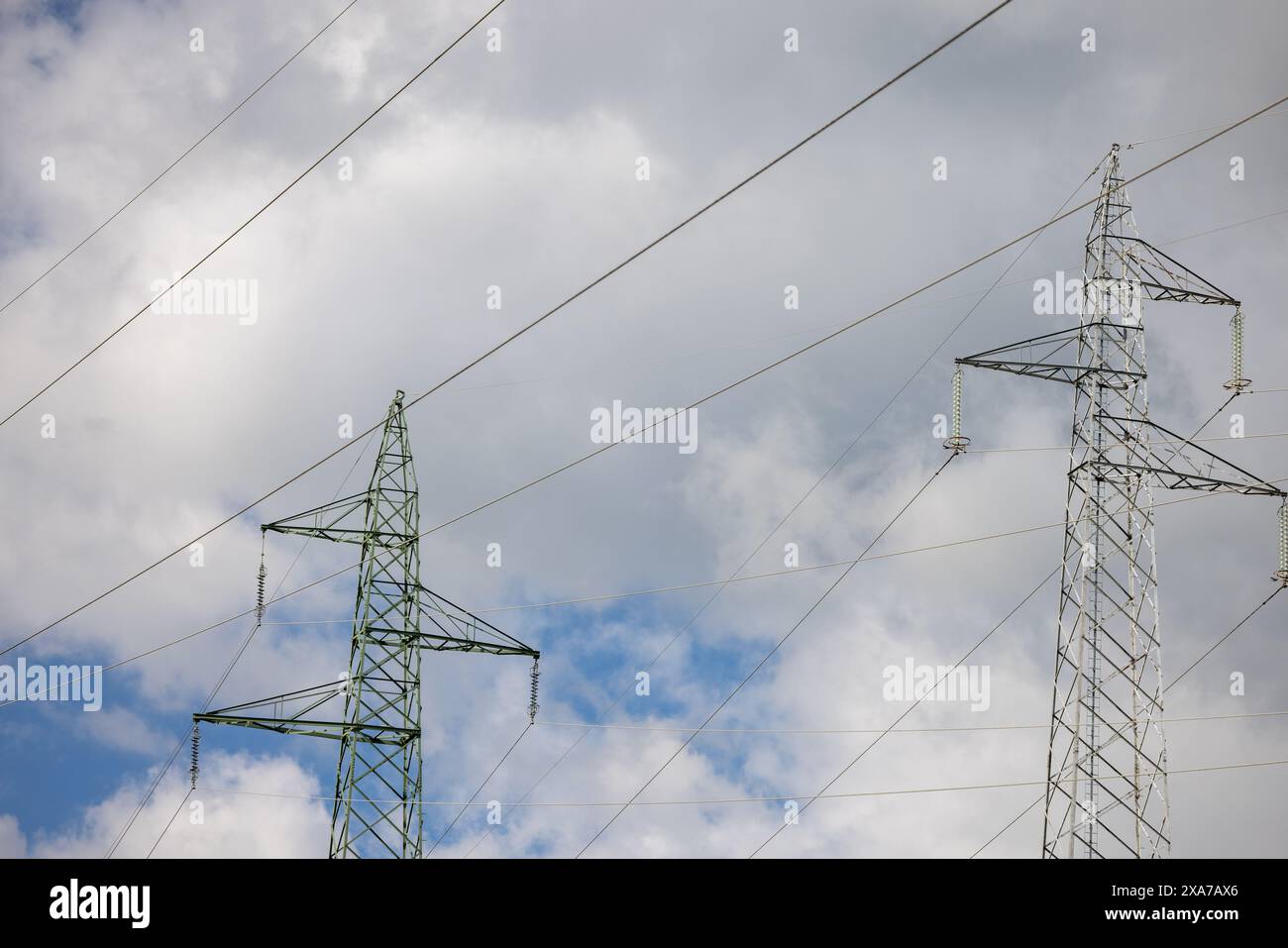 Two towering electricity pylons against a blue sky with white clouds ...