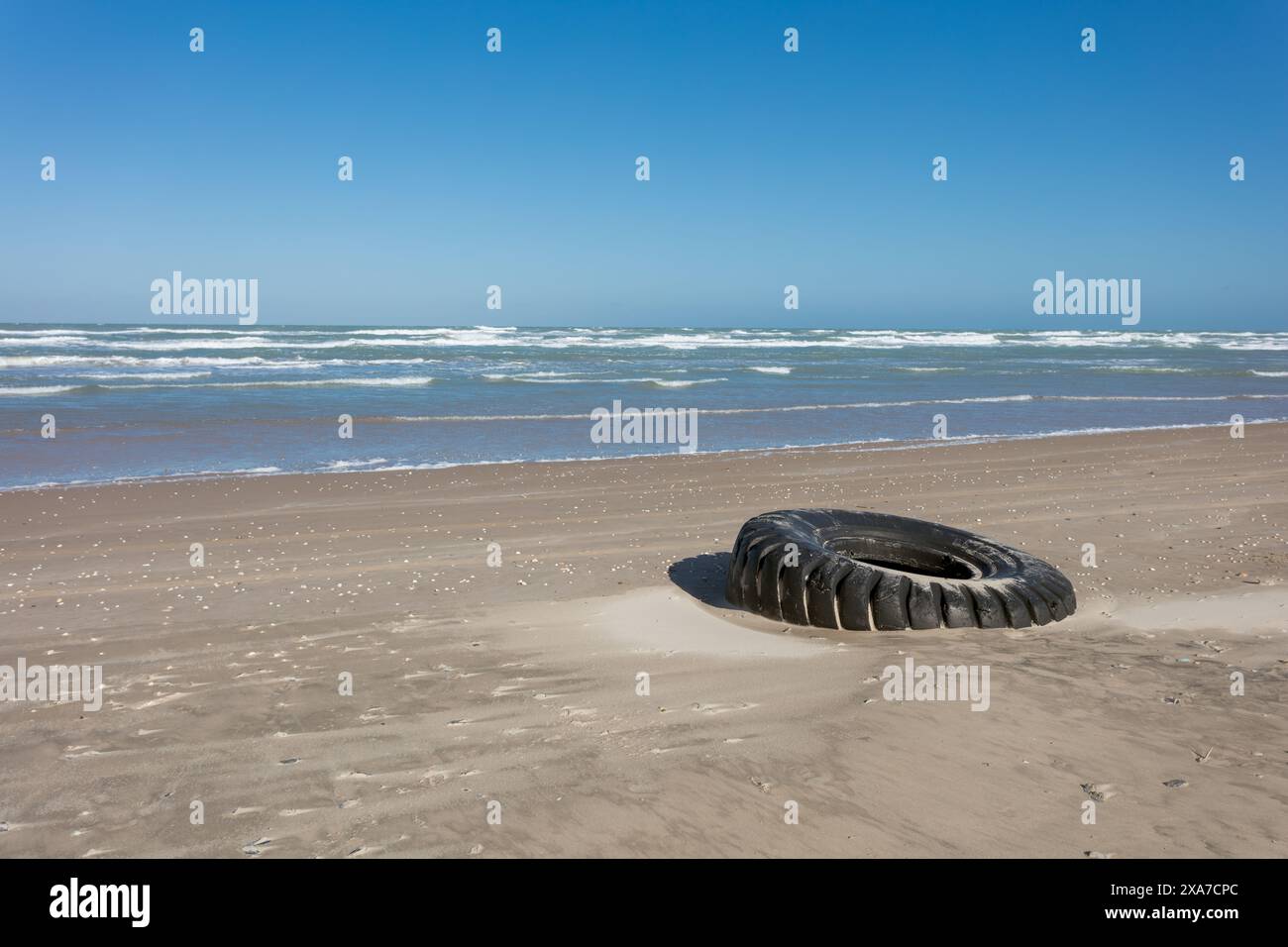 Ocean waves washing up in distance with a tire stuck in sand on the ...