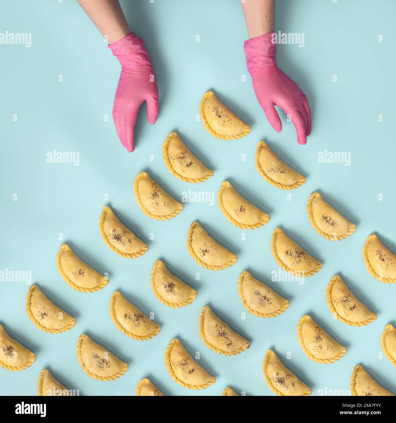 A baker's hands in a pink rubber gloves lays out raw samosa on blue ...