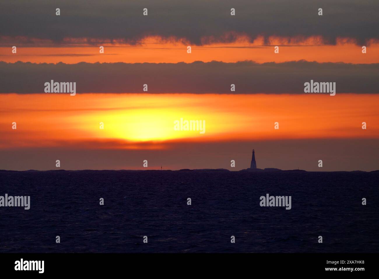 Sun setting behind lighthouse over water and clouds Stock Photo - Alamy