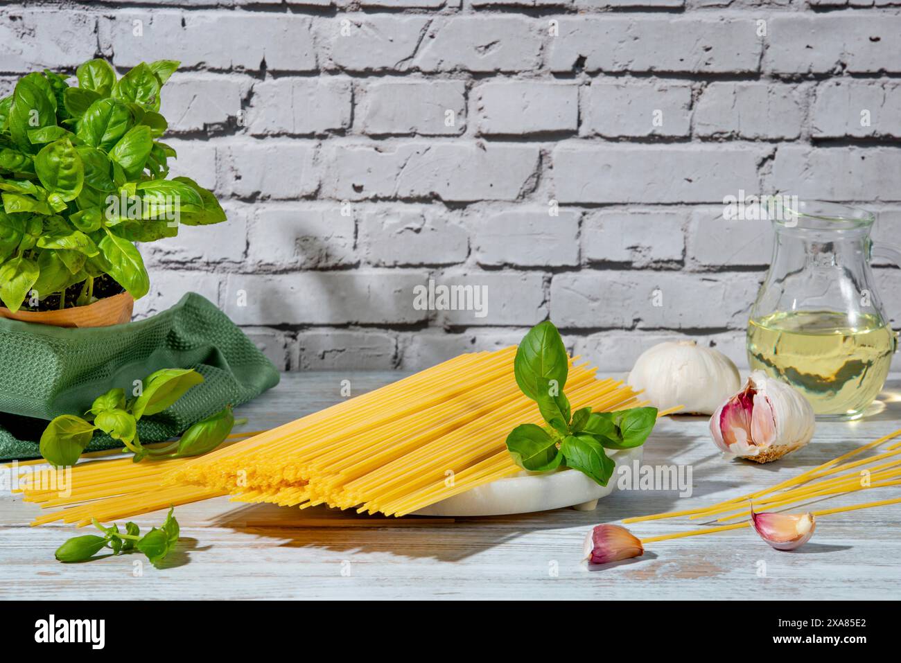 Basil, spaghetti, olive oil and garlic on a table in front of a white ...