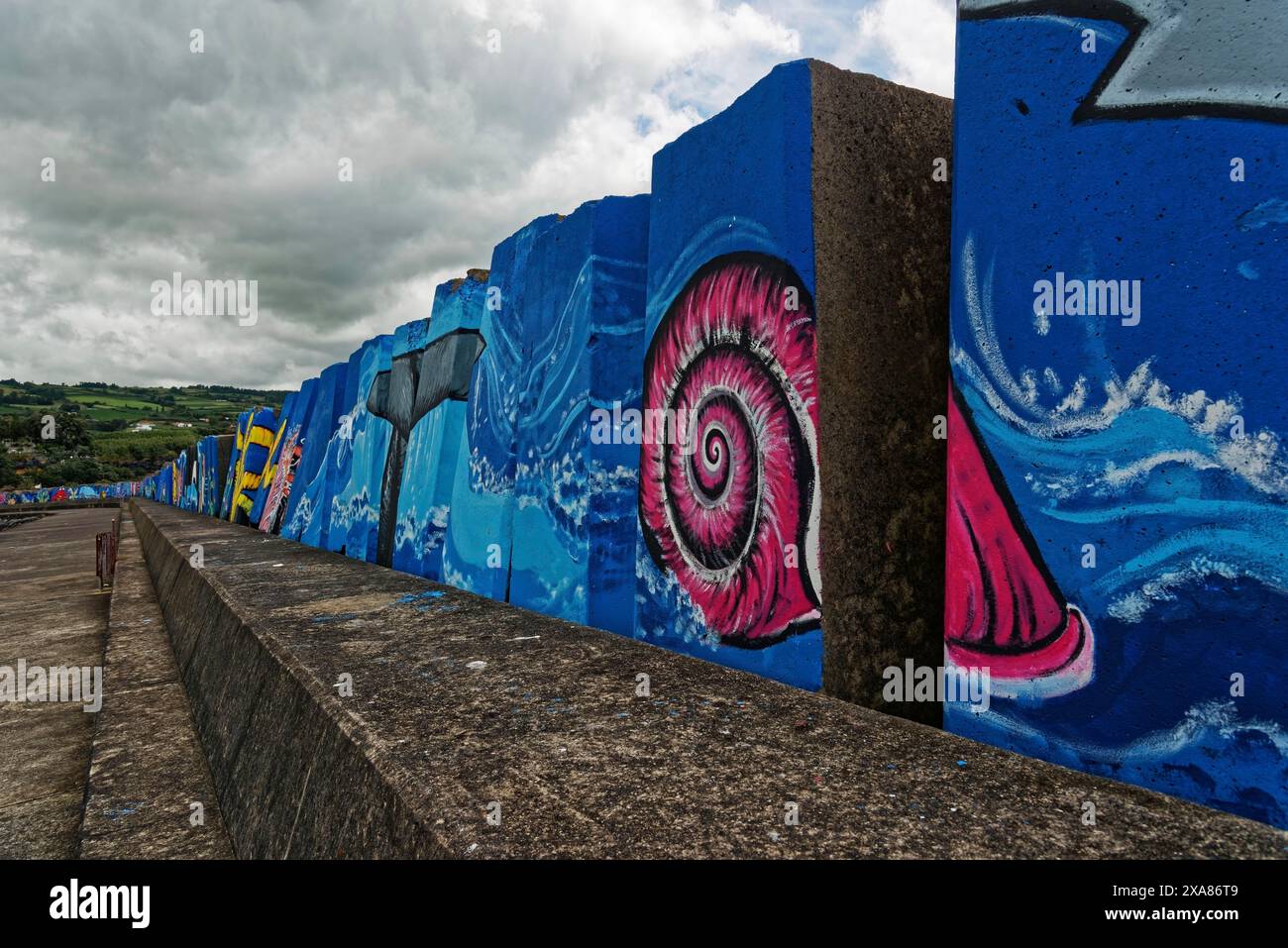 Colourful mural by the sea with a large pink snail under a cloudy sky ...