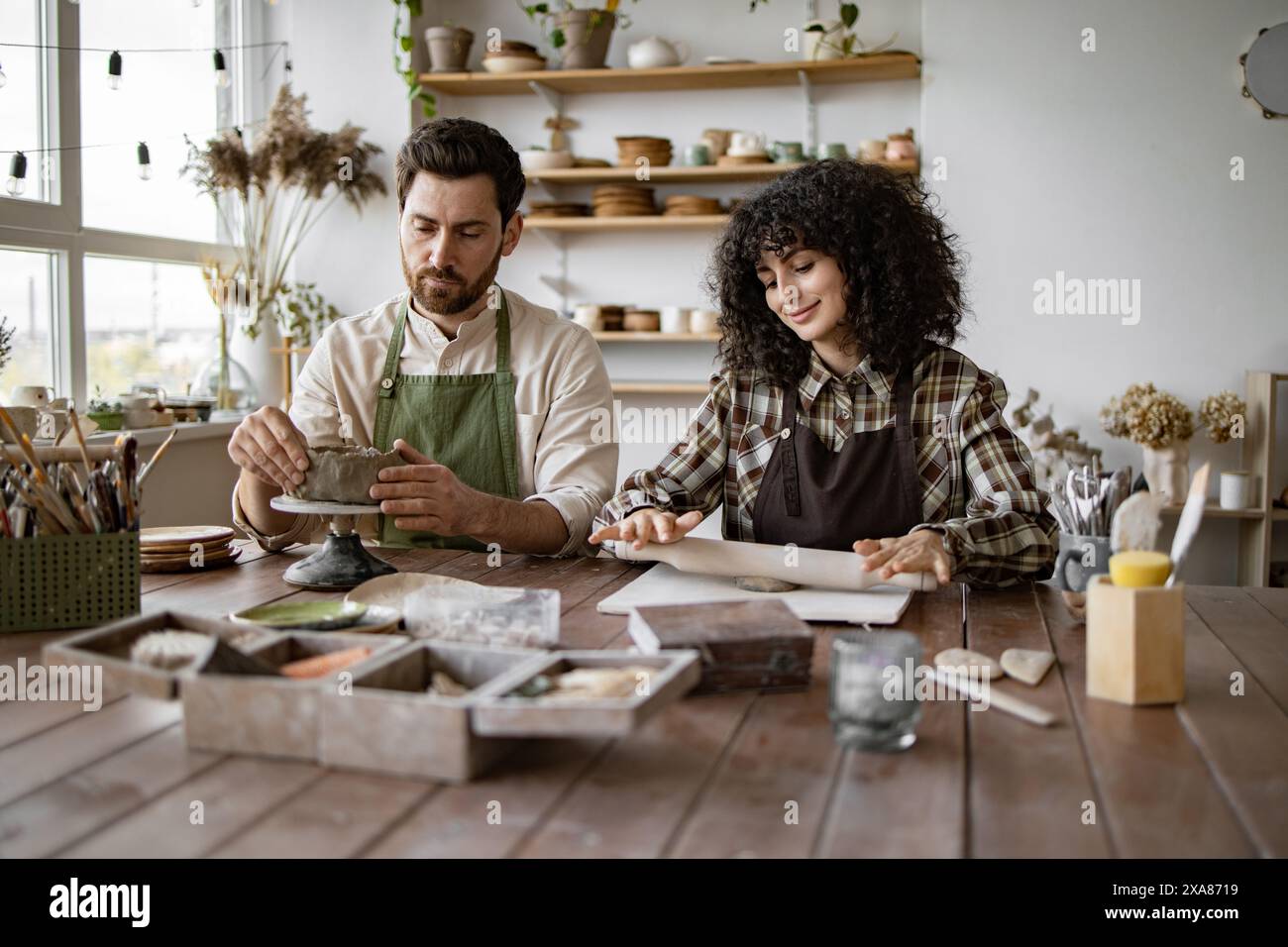 Man sculpting vase and woman rolling clay in pottery studio Stock Photo ...
