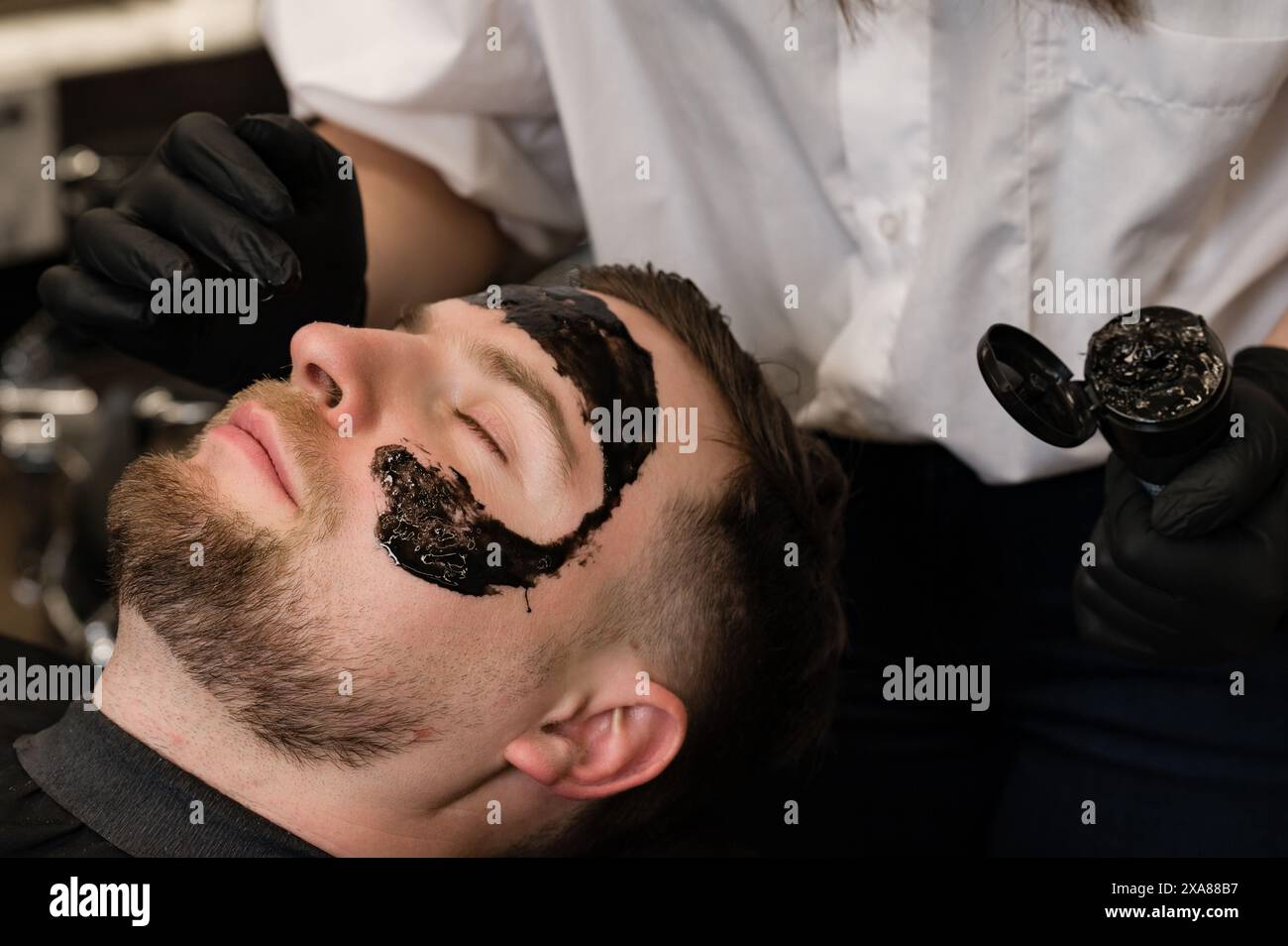Barber applies a black moisturizing mask to a mans face while shaving ...