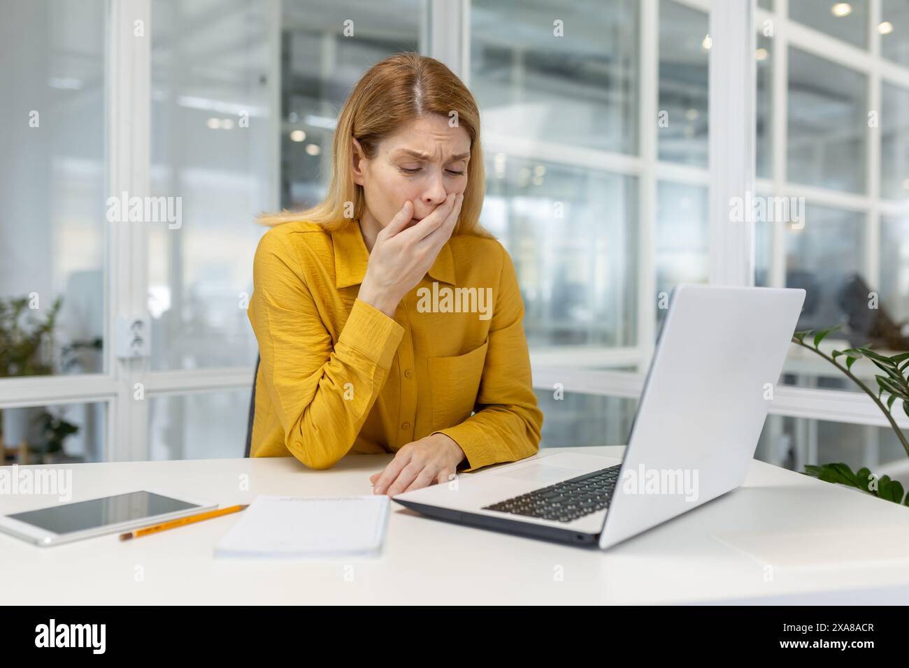 Tired businesswoman yawning while working on a laptop in a modern ...