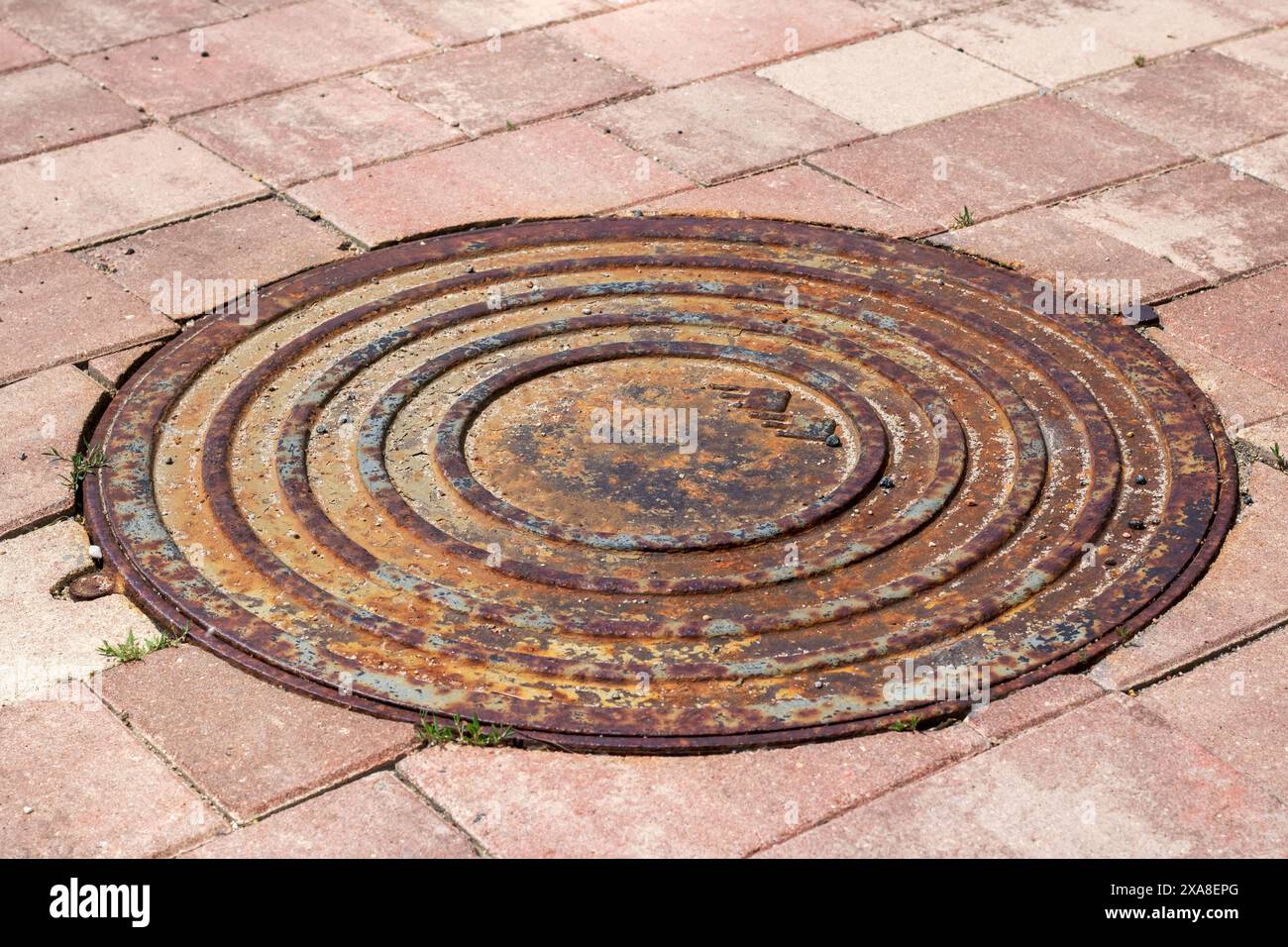 A weathered manhole cover rests upon a brick sidewalk, showcasing a mix of materials. The ...