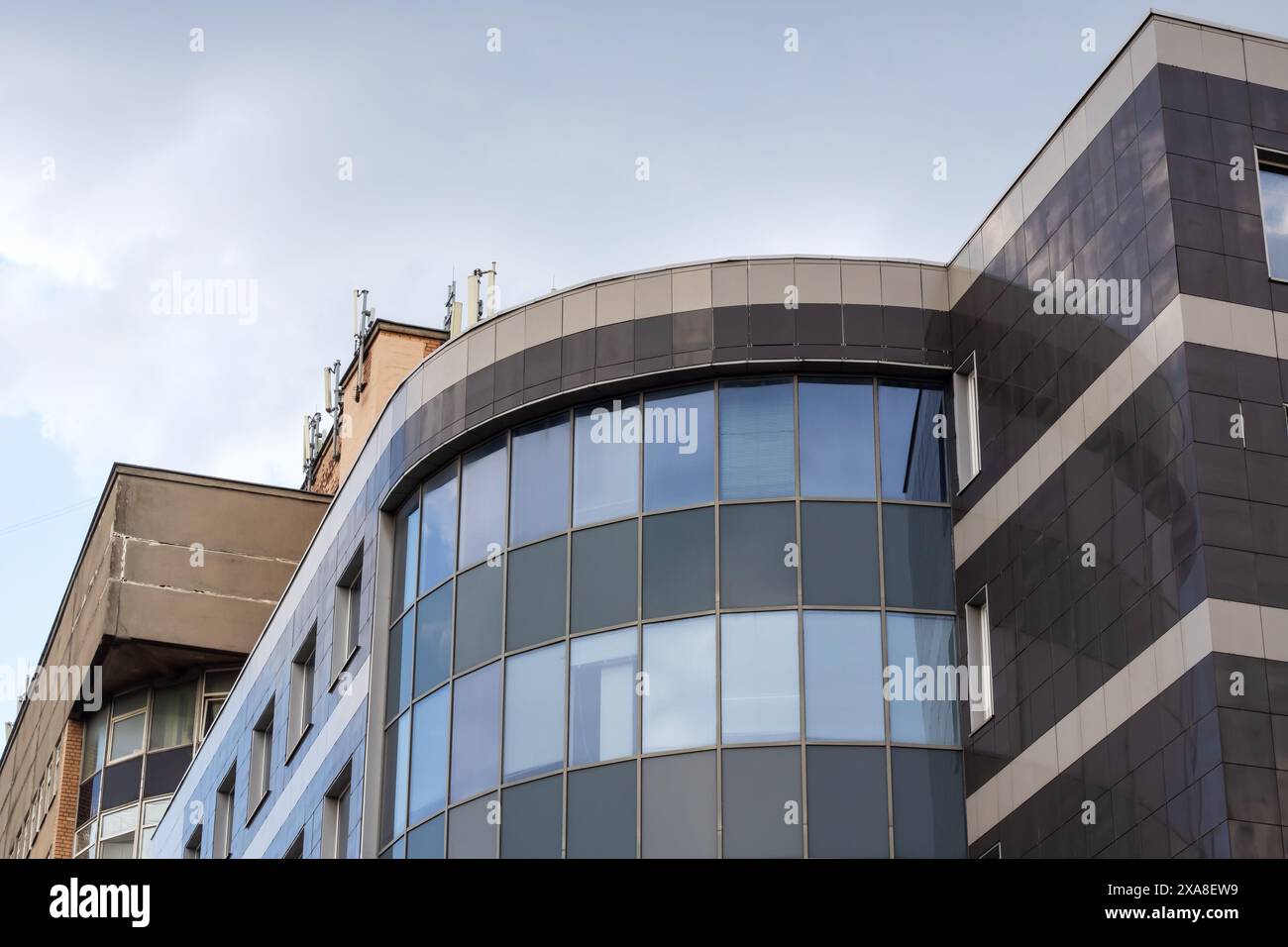 A modern curved building with many windows, against a cloudy urban sky ...