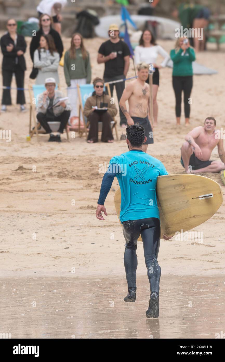 A surfer carrying his surfboard running out of the sea after competing ...