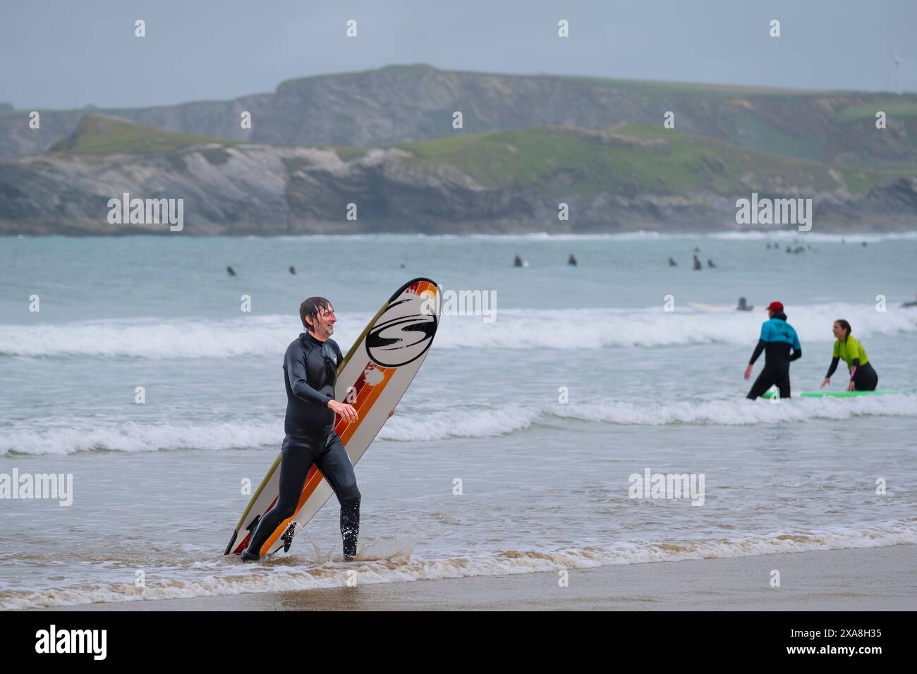 A happy smiling male surfer carrying his surfboard and walking out of ...