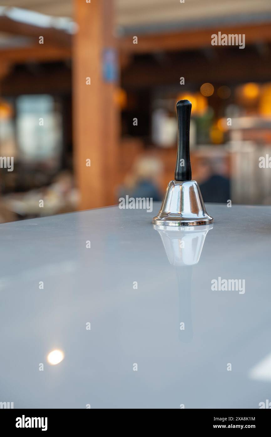A silver bell sits on a white countertop. The bell is black and shiny ...