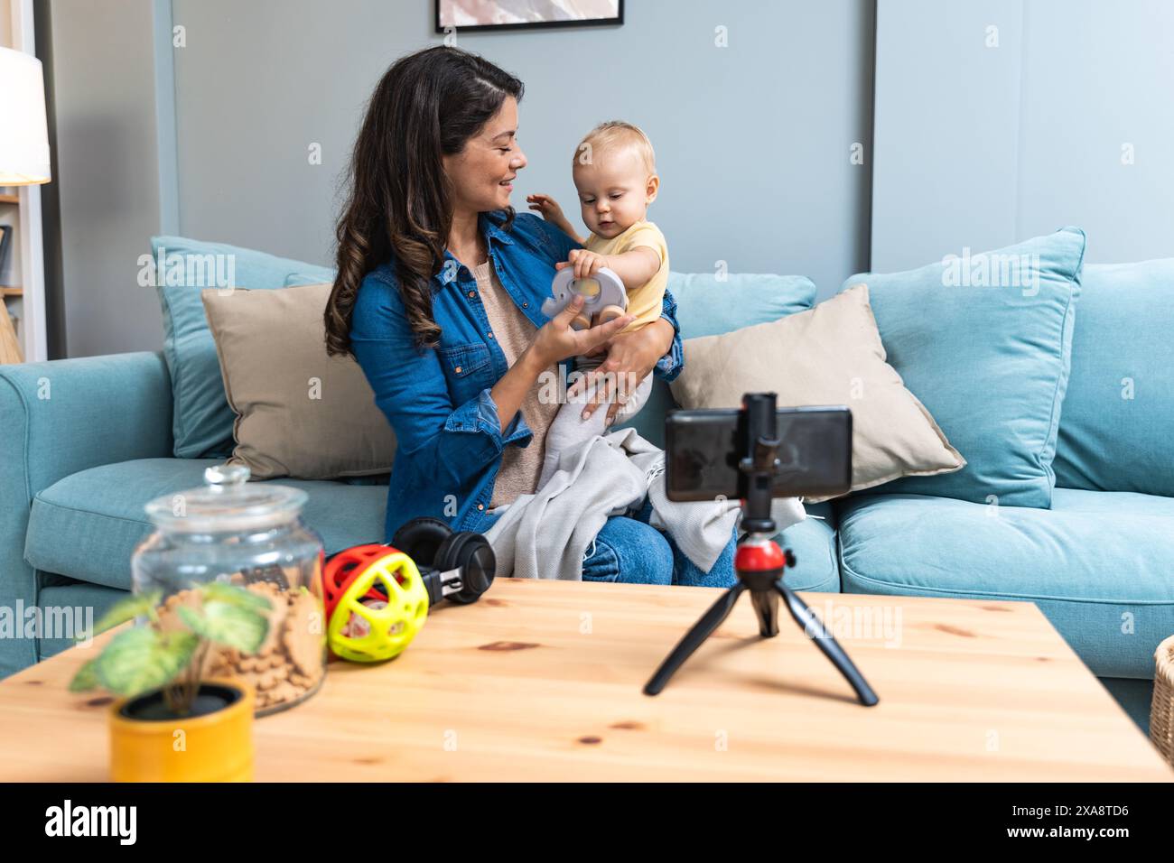 Young mother with baby sitting at sofa with child on her lap trying to ...