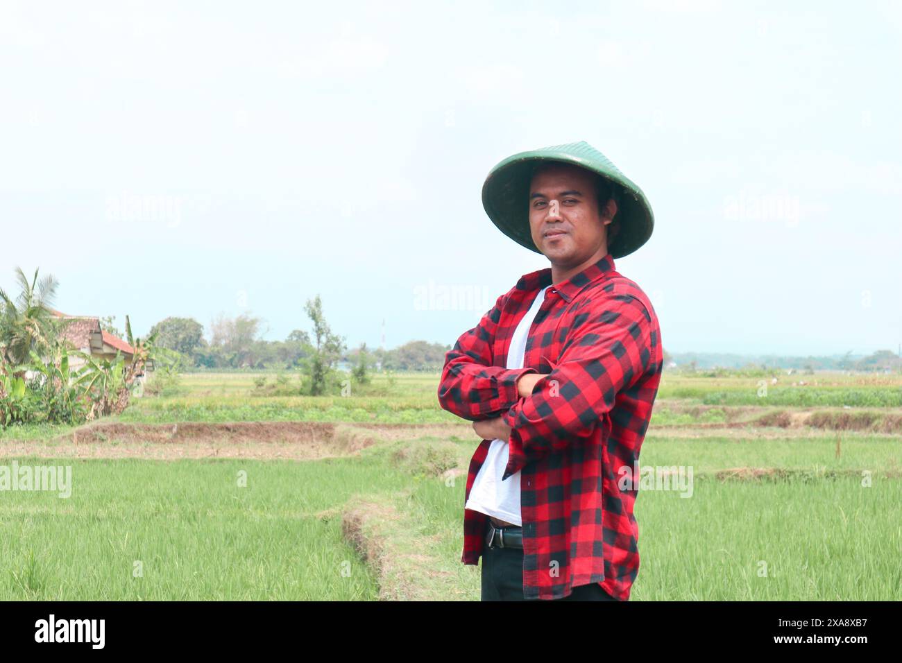 Portrait of a shocked Asian male farmer wearing a hat, holding his ...