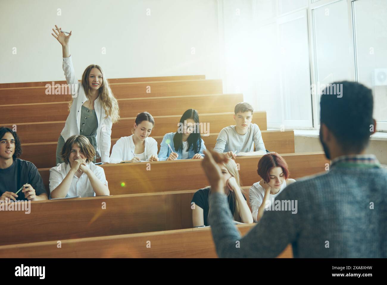Young girl raising hand to give answer to the teacher during lesson ...