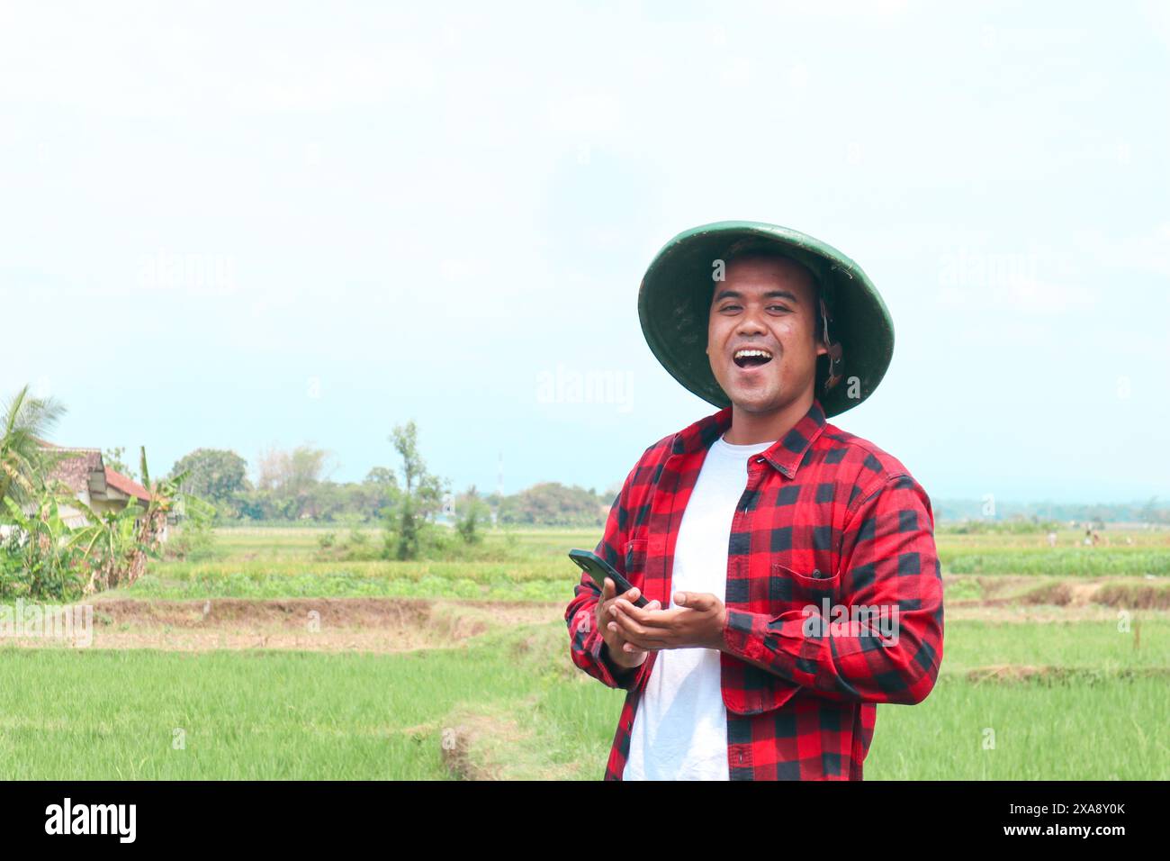 Portrait of a shocked Asian male farmer wearing a hat, holding his ...