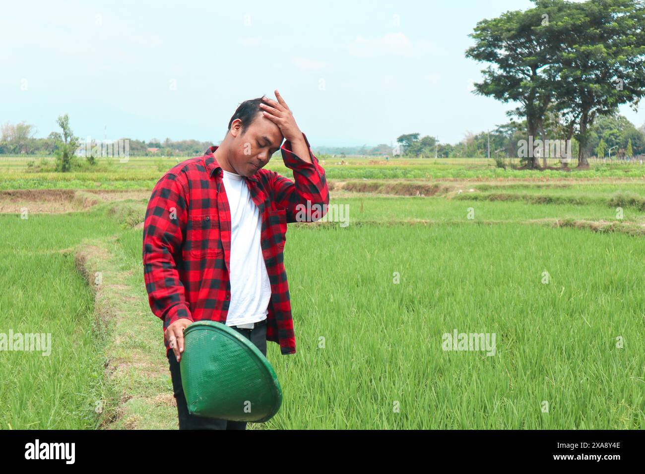 Portrait of a shocked Asian male farmer wearing a hat, holding his ...