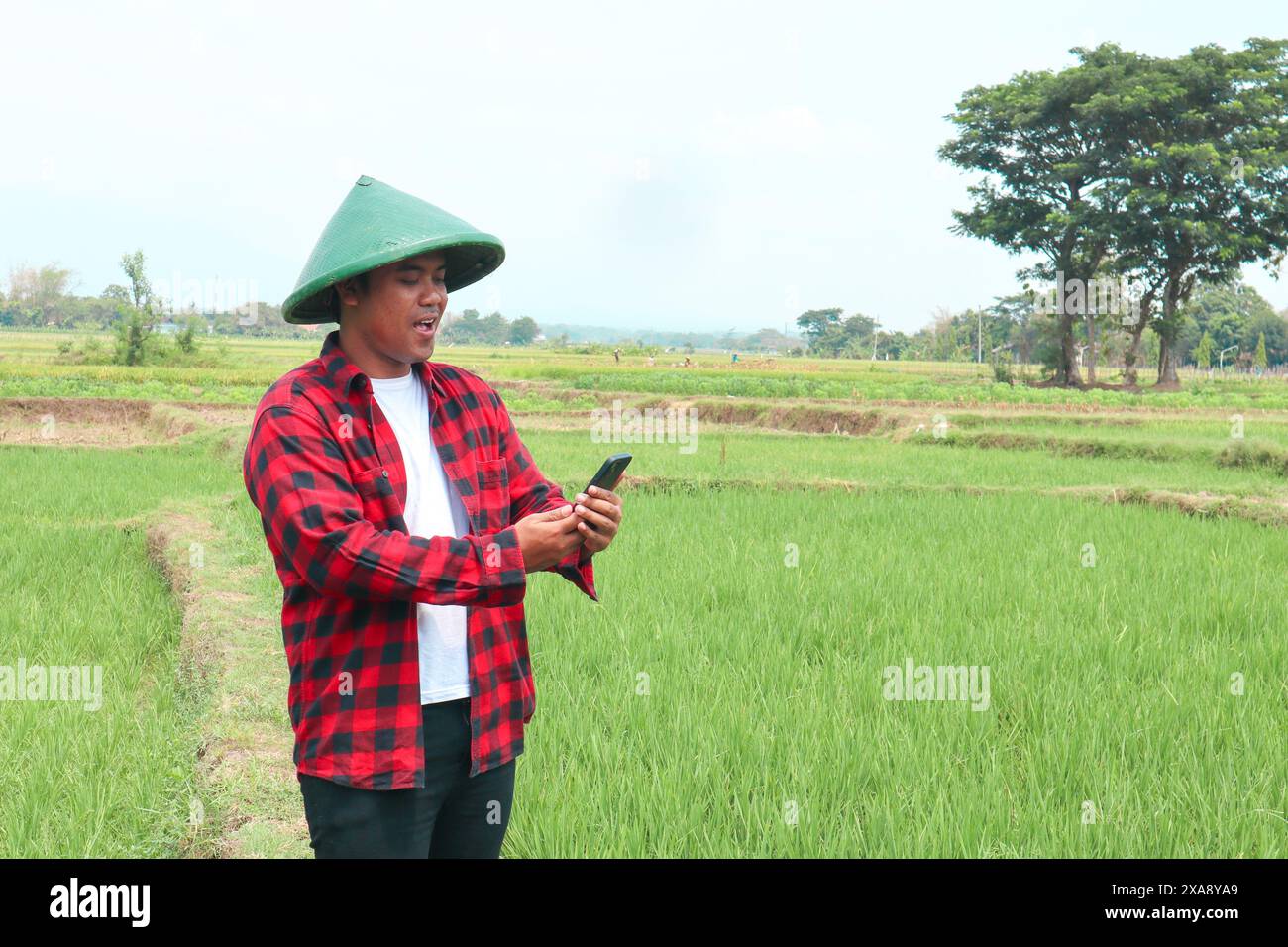 Portrait of a shocked Asian male farmer wearing a hat, holding his ...