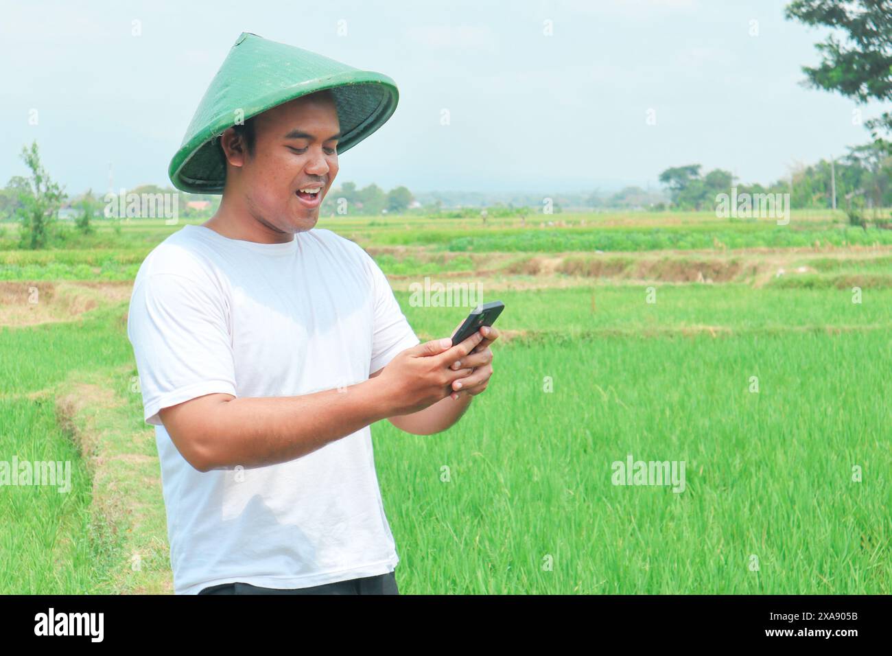 Portrait of a shocked Asian male farmer wearing a hat, holding his ...