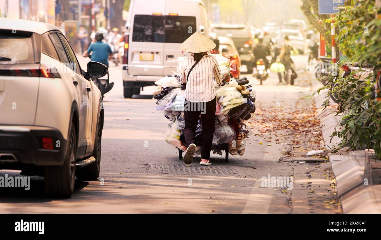 In the bustling cityscape of Hanoi, a street vendor wearing a straw hat ...