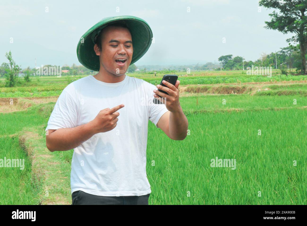Portrait of a shocked Asian male farmer wearing a hat, holding his ...
