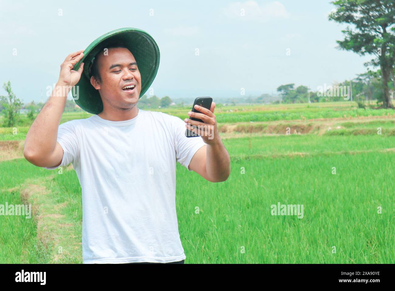 Portrait of a shocked Asian male farmer wearing a hat, holding his ...