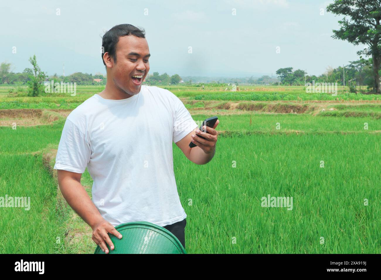 Portrait of a shocked Asian male farmer wearing a hat, holding his ...